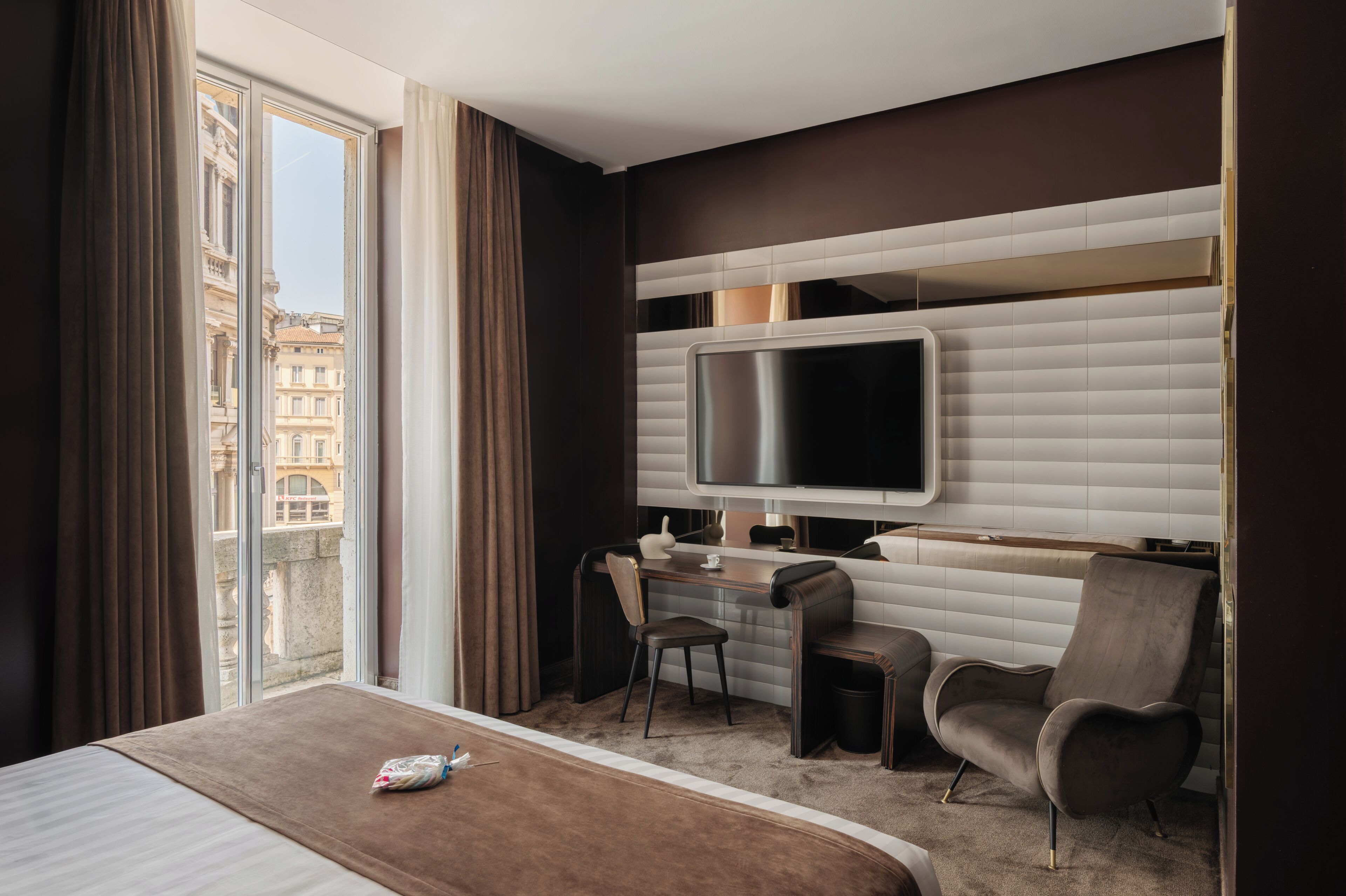 Quarto de hotel com cama, escrivaninha, cadeira, televisão e vista para edifícios.