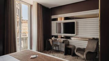 Quarto de hotel com cama, escrivaninha, cadeira, televisão e vista para edifícios.