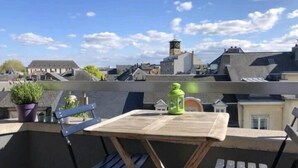 Terraço no telhado com mesa e cadeiras de madeira, um candeeiro verde e vista para a paisagem urbana, incluindo uma torre do relógio.