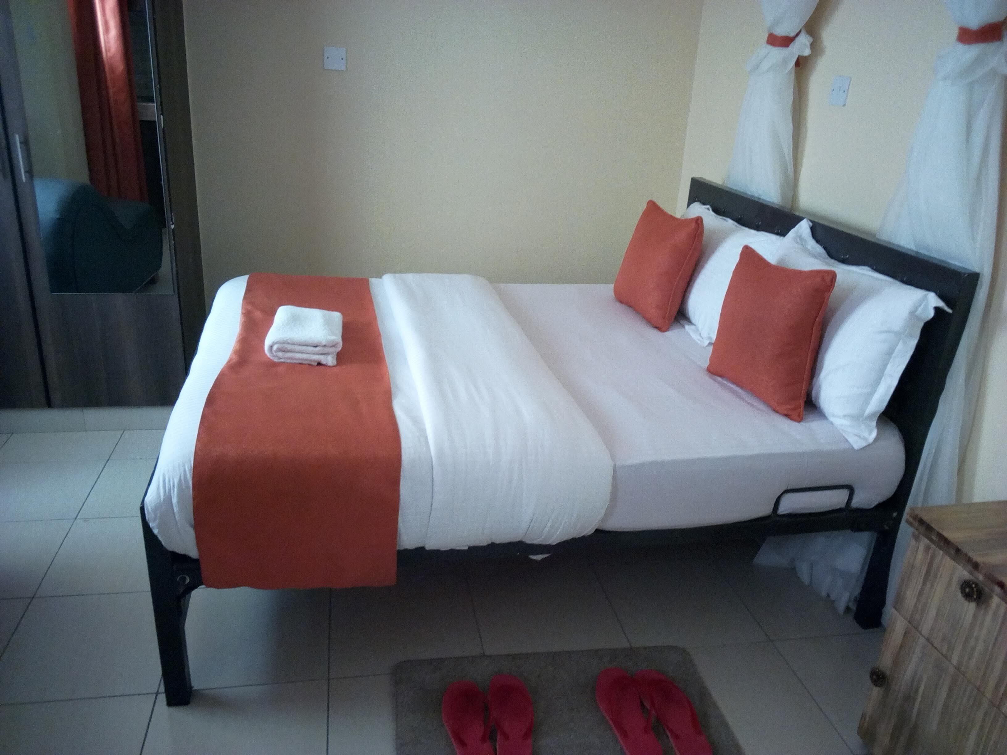 Uma cama de solteiro com um edredom vermelho e branco, duas almofadas vermelhas e brancas, e uma toalha branca dobrada sobre a cama.