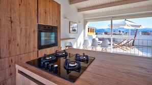 Uma cozinha moderna com ilha central, armários de madeira, forno embutido e uma grande porta de vidro deslizante que dá para uma varanda com área de estar ao ar livre.