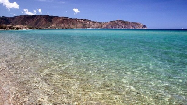 Uma praia tranquila com águas rasas e uma montanha ao fundo.