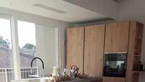 Uma cozinha moderna com armários de madeira, forno embutido e um espaço de jantar com cadeiras brancas e uma mesa posta para dois.