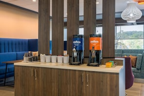 Um balcão com dispensadores de café, uma área de estar com sofá azul e vista para o exterior.