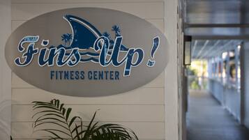 Placa para 'Fins-Up Fitness Center' com um gráfico estilizado de tubarão e palmeiras.