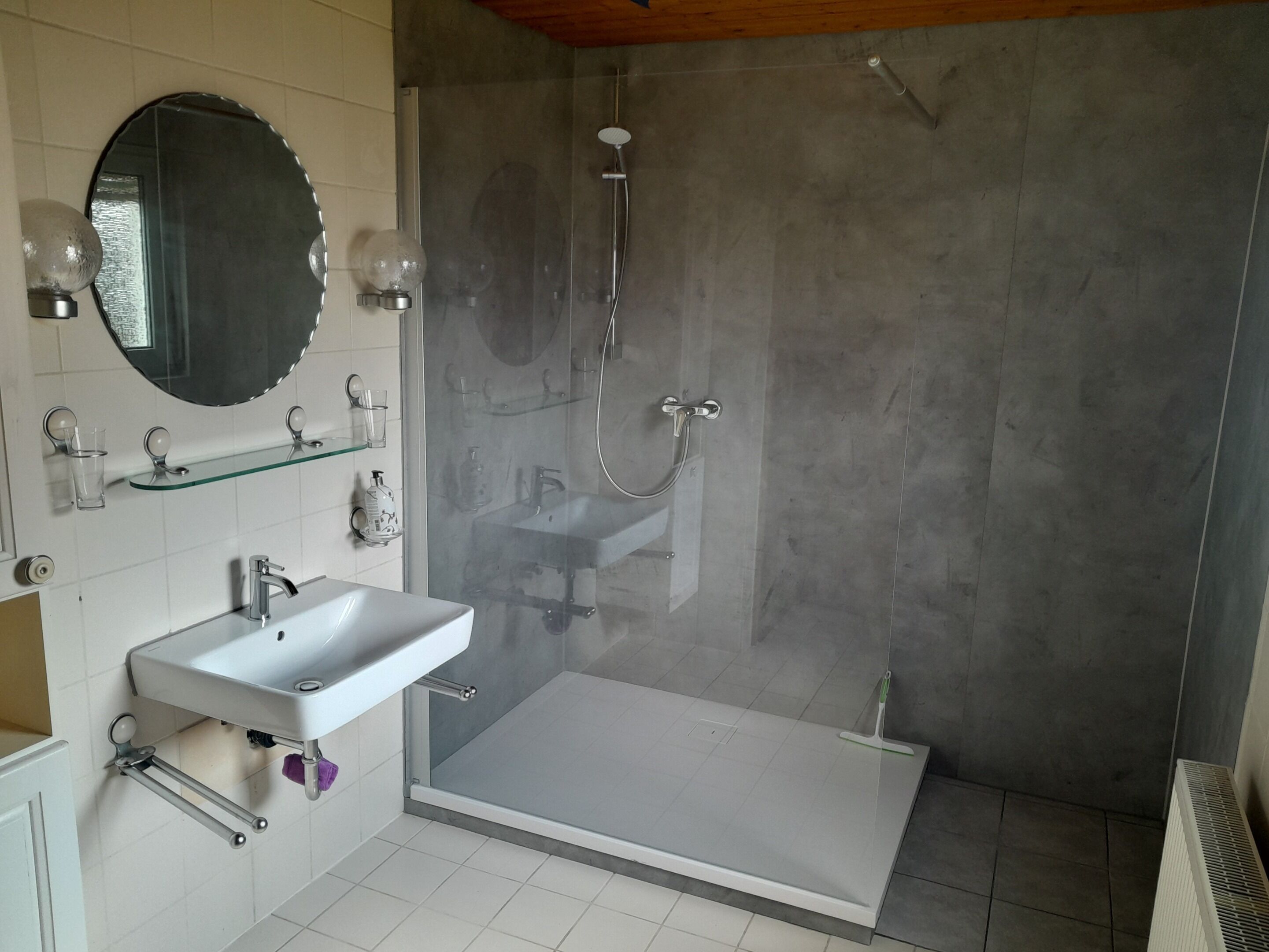 Uma casa de banho moderna com uma pia branca, cabine de duche em vidro e um espelho grande.