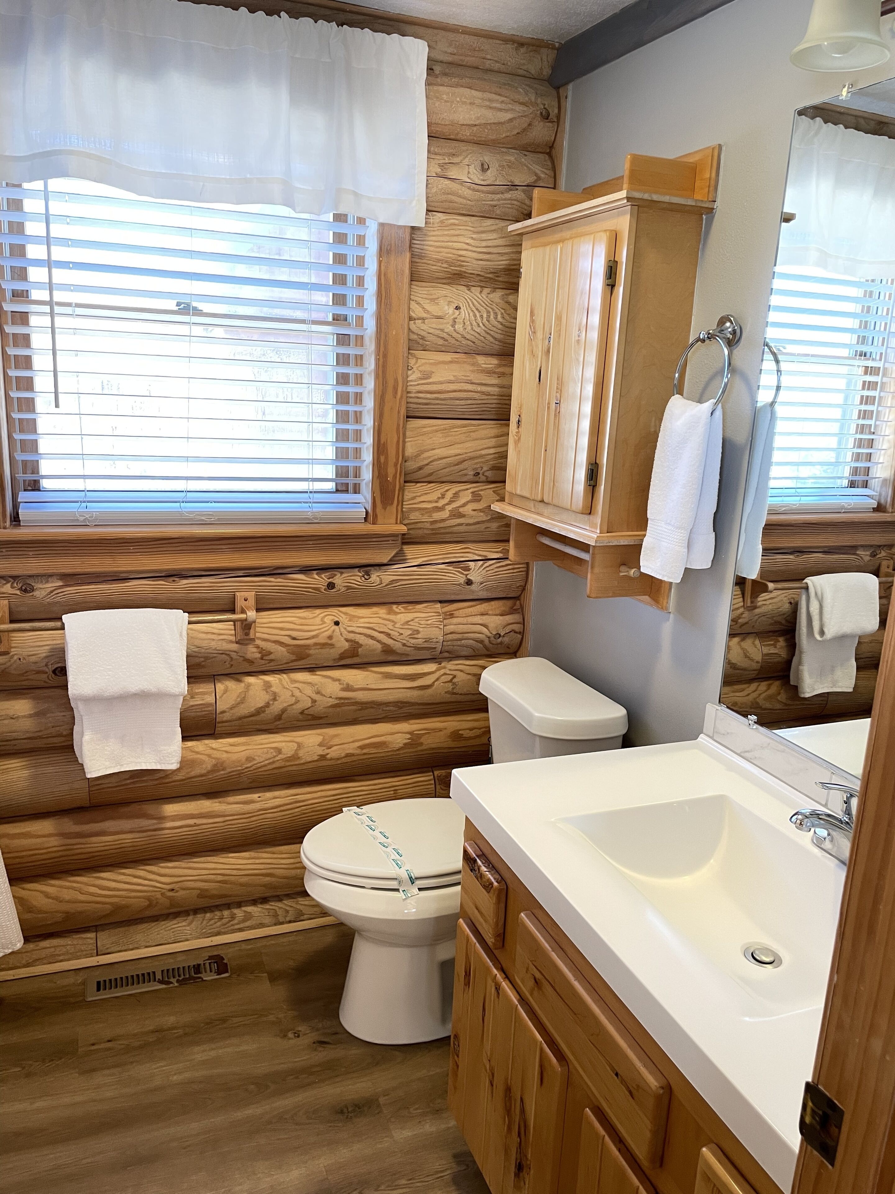 Um banheiro estilo cabana de madeira, com vaso sanitário, pia e armários de madeira.
