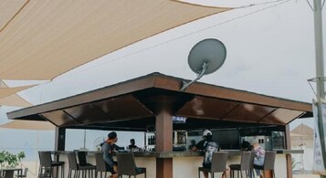 Uma área de bar ao ar livre com antena parabólica, assentos cobertos e um balcão.