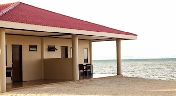 Um edifício à beira-mar com telhado vermelho, área de estar coberta e vista para o mar.