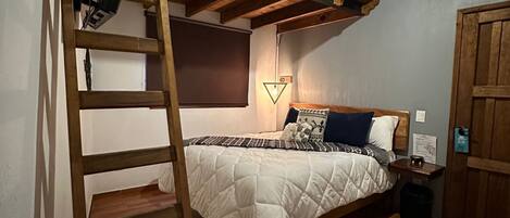 Quarto com cama de solteiro, escada de madeira e mesa de cabeceira com abajur.