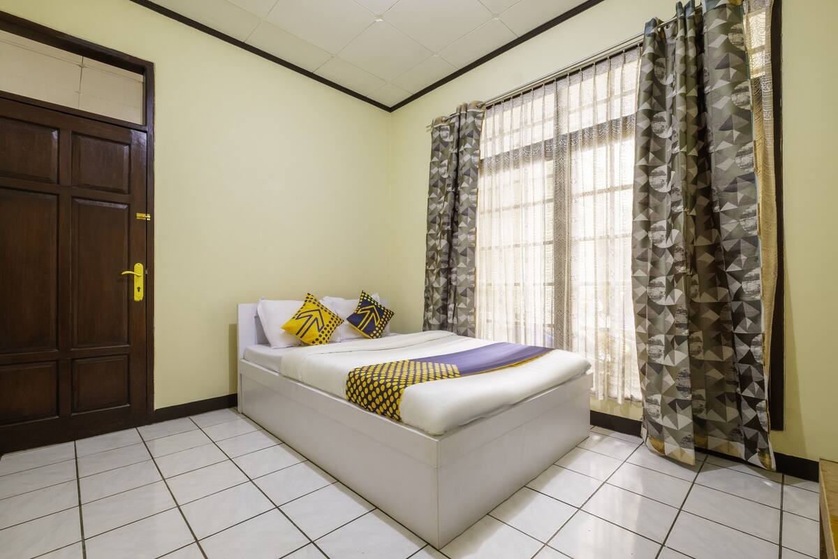 Quarto com cama, cortinas, porta e chão em azulejos.