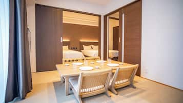 Quarto de hotel com mesa de jantar posta para dois, cama com roupa de cama branca e guarda-roupa de madeira.