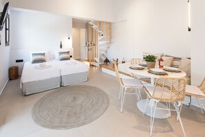 Um quarto moderno e minimalista com duas camas, um espaço de refeições com cadeiras de vime e uma escada.