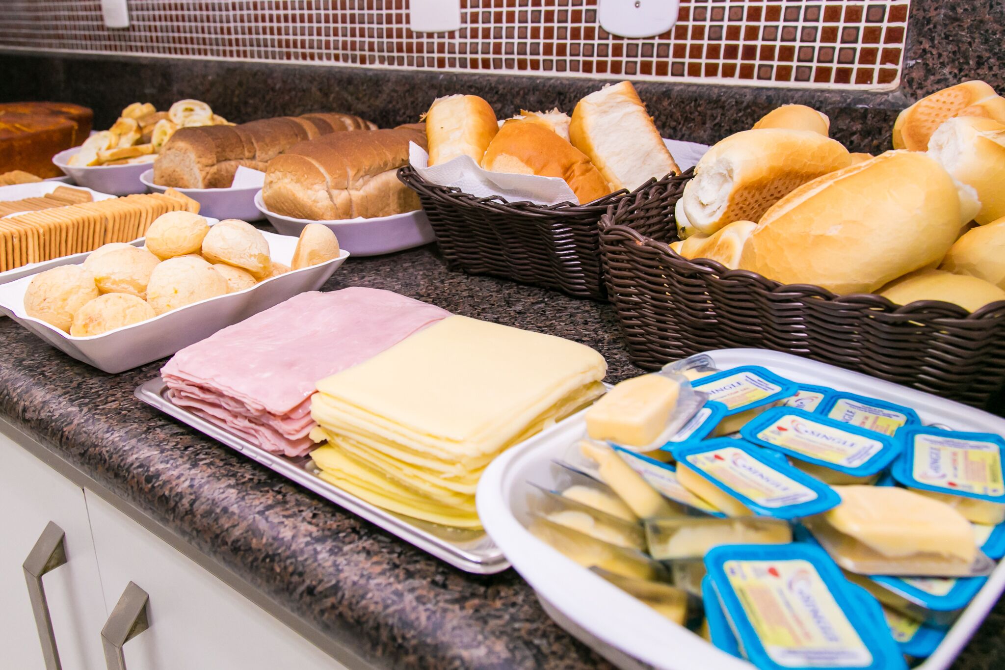Buffet com diversos itens de comida, incluindo pão, doces e queijo.
