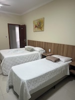 Quarto de hotel com duas camas de solteiro, cabeceira de madeira, um quadro na parede e uma porta.