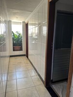 Um corredor com paredes e chão revestidos de azulejos, uma planta em vaso e uma porta.