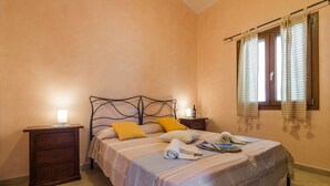 Quarto com cama, mesas de cabeceira, abajur, janela com cortinas e uma porta na parede.