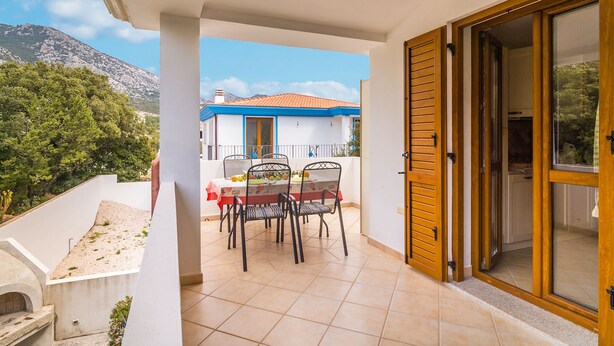 Uma varanda com mesa e cadeiras, uma porta de madeira e vista para uma casa com telhado azul.