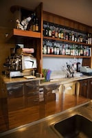 Uma área de bar com uma máquina de café, prateleiras cheias de garrafas de bebidas e uma pia.