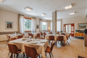 Uma área de refeições com várias mesas e cadeiras, amplas janelas e vista para o exterior.