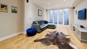 Uma sala de estar moderna com piso em padrão herringbone, um sofá seccional, um pufe azul e um tapete de couro grande.