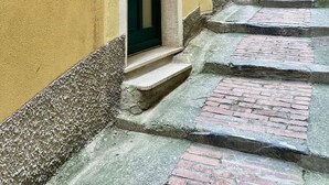 Uma rua estreita com um edifício amarelo, uma porta verde e uma escadaria de tijolos.