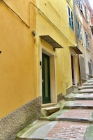 Uma rua estreita com edifícios amarelos, uma porta verde e um caminho de tijolos.
