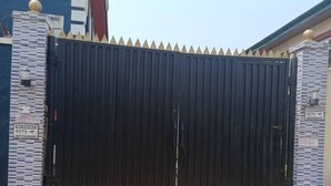 Uma entrada com portão, placa de aviso de vigilância por circuito fechado, um poste de metal e um edifício com a inscrição 'Hotel' ao fundo.
