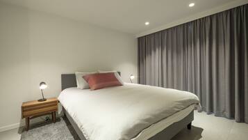 Quarto moderno com cama grande, mesa de cabeceira com abajur e janela com cortinas.