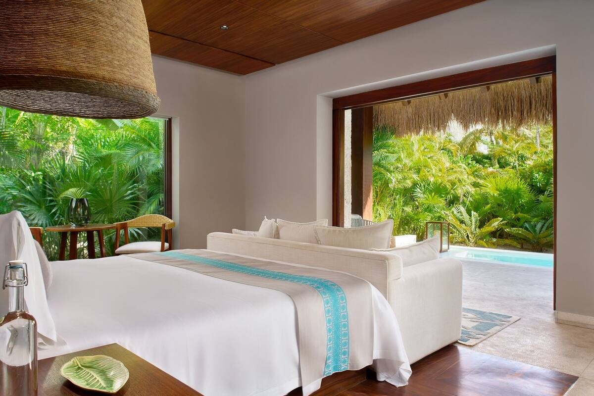Quarto com cama, sofá, uma janela grande e vista para o verde.