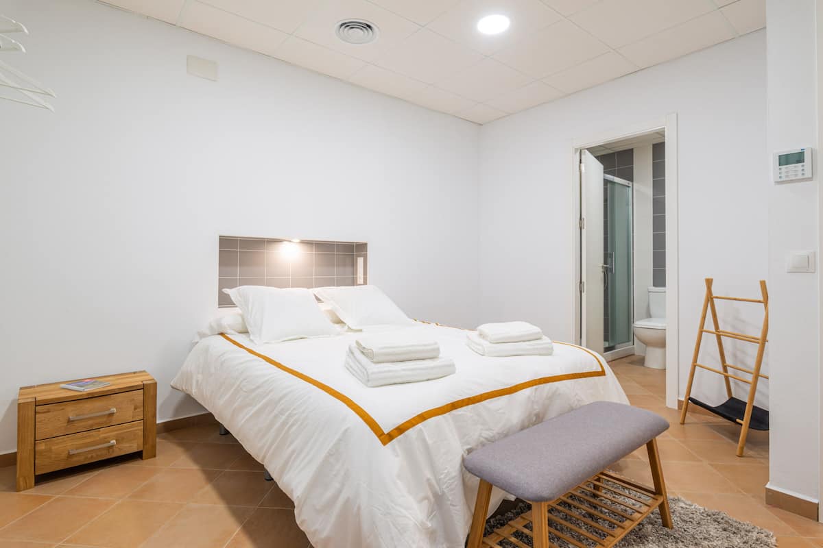 Quarto bem arrumado com cama, mesa de cabeceira e um banquinho.