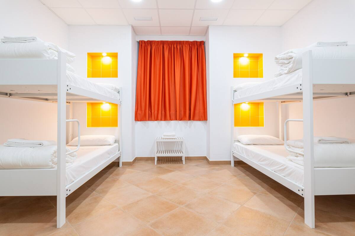 Um quarto com beliches, uma pequena mesa branca e luzes laranja nas paredes.