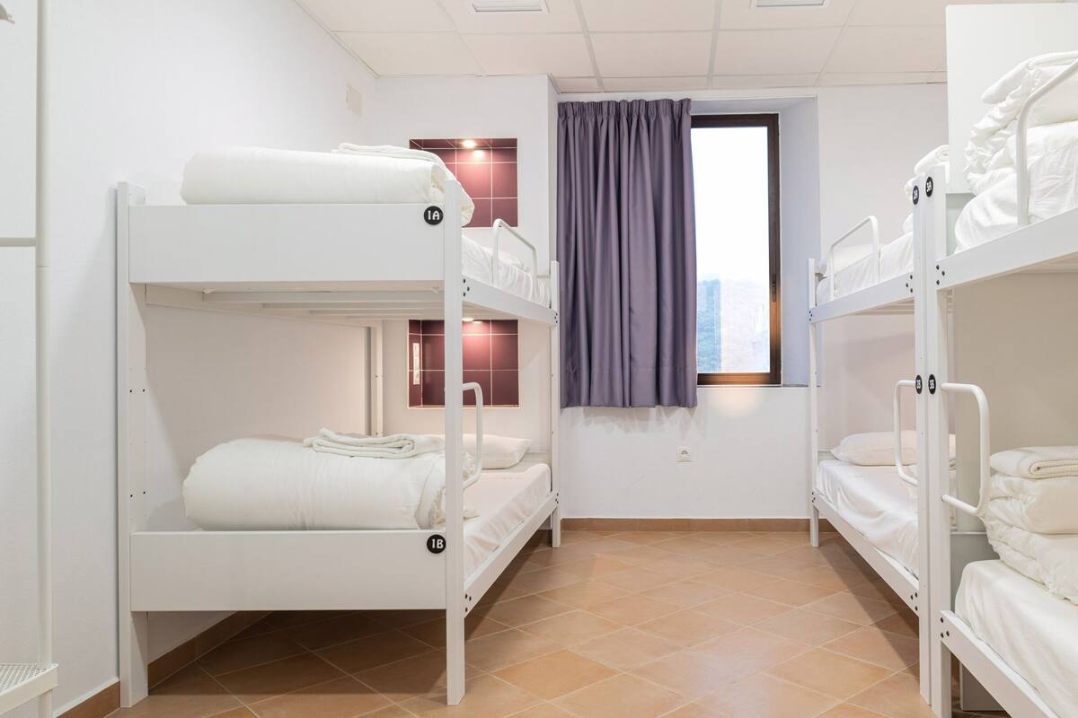 Um dormitório com beliches, uma janela com cortinas e piso de azulejos.