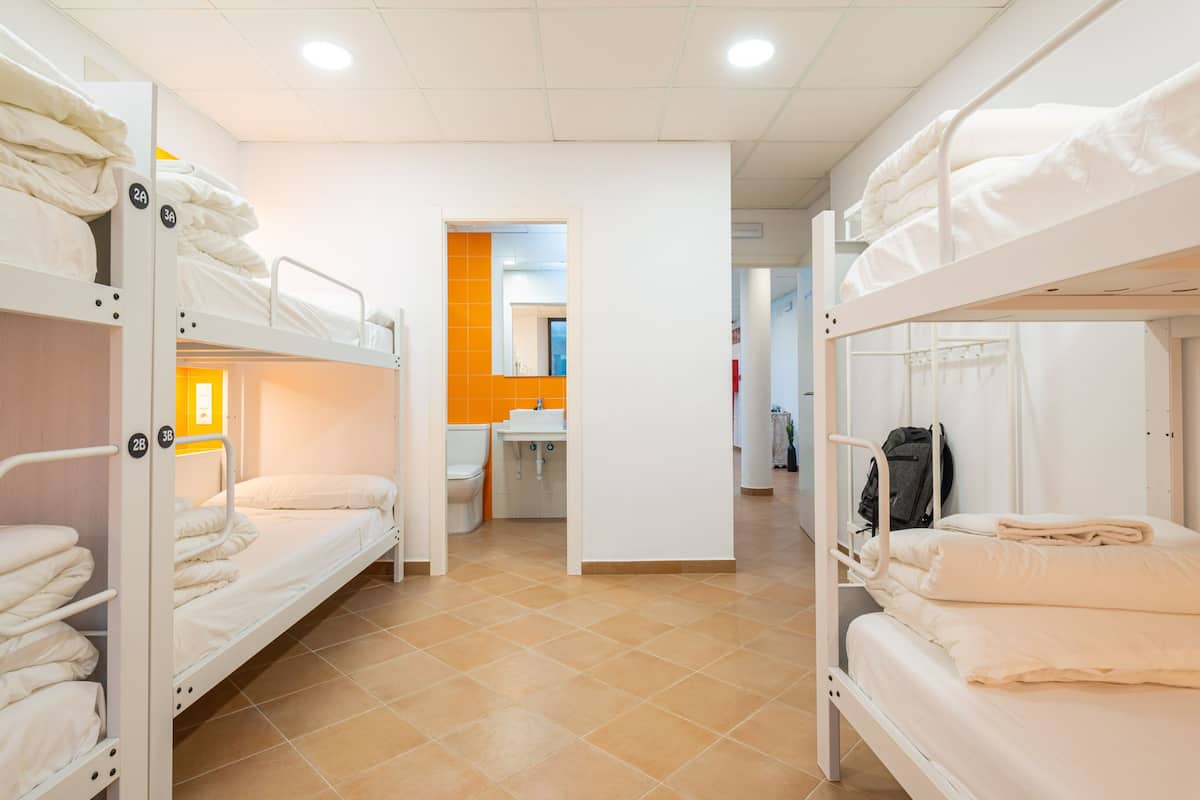 Quarto tipo dormitório com beliches, banheiro com azulejos laranja e pia.