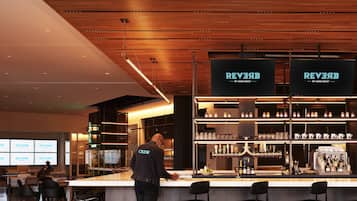 Uma área de bar moderna com um bartender, teto de madeira e banquetas.