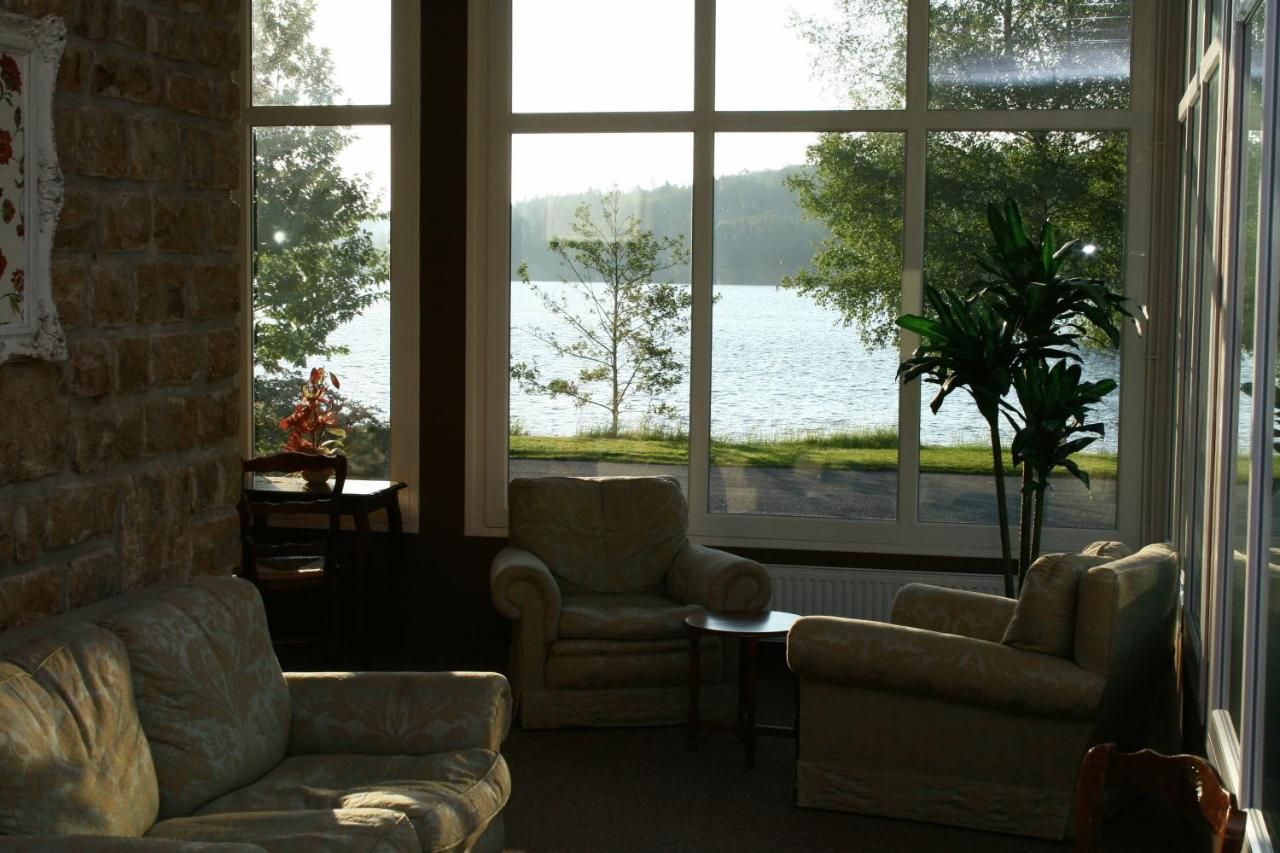 Um quarto acolhedor com uma grande janela com vista para um lago, mobiliado com um sofá, cadeiras e uma mesa pequena.