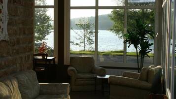 Um quarto acolhedor com uma grande janela com vista para um lago, mobiliado com um sofá, cadeiras e uma mesa pequena.