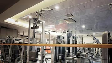 Academia com diversos aparelhos de ginástica e um corrimão de madeira em primeiro plano.