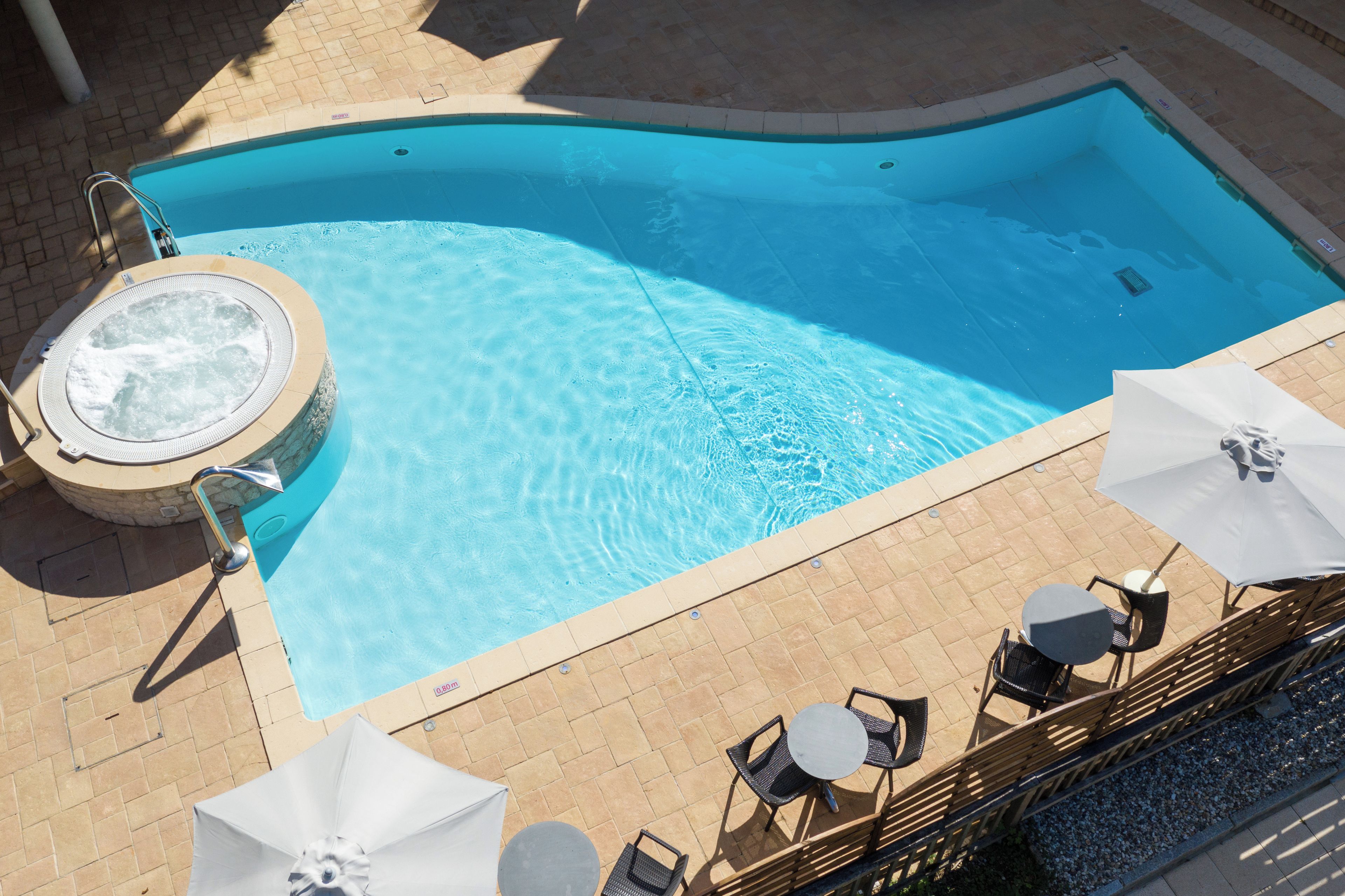 Piscina com hidromassagem, rodeada por áreas de estar ao ar livre e guarda-sóis.