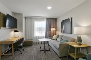 Quarto de hotel com uma escrivaninha, um sofá, uma mesa redonda e uma televisão fixada na parede.