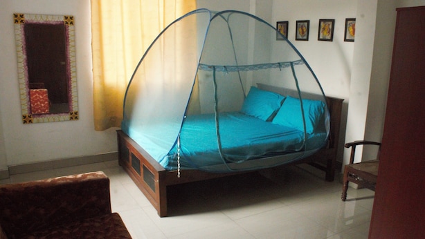 Quarto com uma cama sob um mosquiteiro, uma cadeira e um espelho na parede.