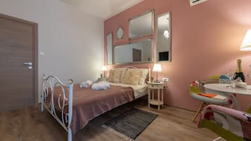 Quarto com cama, mesas de cabeceira, espelho, cadeira e uma pequena mesa com abajur.