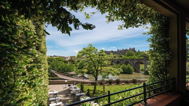 Terraço com área de estar ao ar livre, com vista para uma ponte histórica e rio.