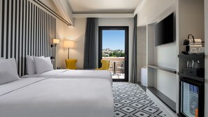 Quarto de hotel com duas camas, televisão, minibar e varanda com vista para a cidade.