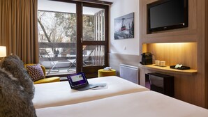 Quarto de hotel com uma cama, um laptop, uma cafeteira e uma televisão na parede.