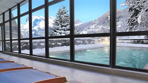 Quarto com amplas janelas com vista para uma paisagem montanhosa nevada e uma piscina.