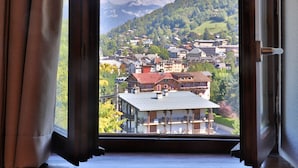 Janela com cortinas, vista de uma cidade com edifícios e uma montanha ao fundo.