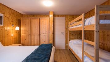 Quarto de madeira com beliches, uma cama de solteiro e um guarda-roupa.