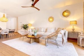 Uma sala de estar moderna com um sofá branco, cadeiras de vime, uma mesa de centro de madeira e um ventilador de teto.