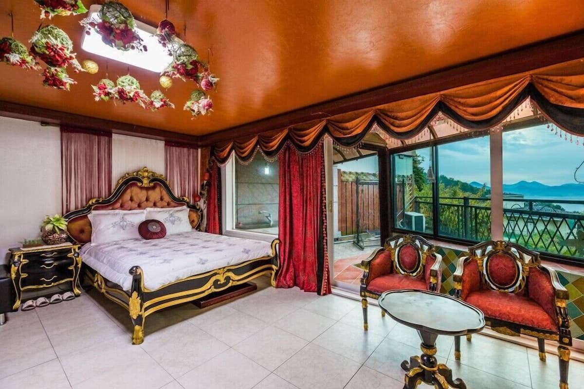 Quarto com cama grande, sofá e varanda com vista.